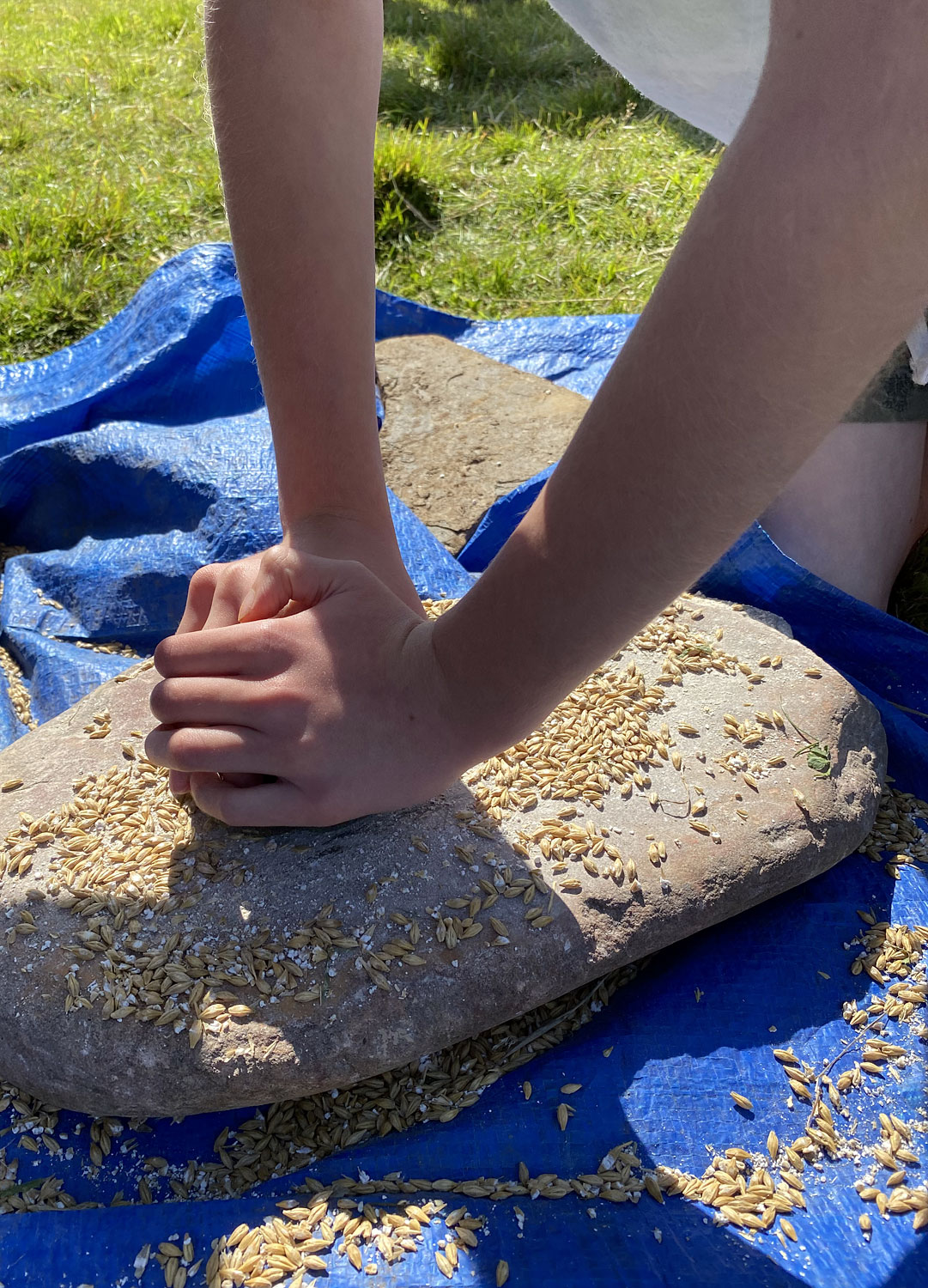 Calum from Essex grinding grain on a saddle quern. (📷 Jo Bourne) – The ...